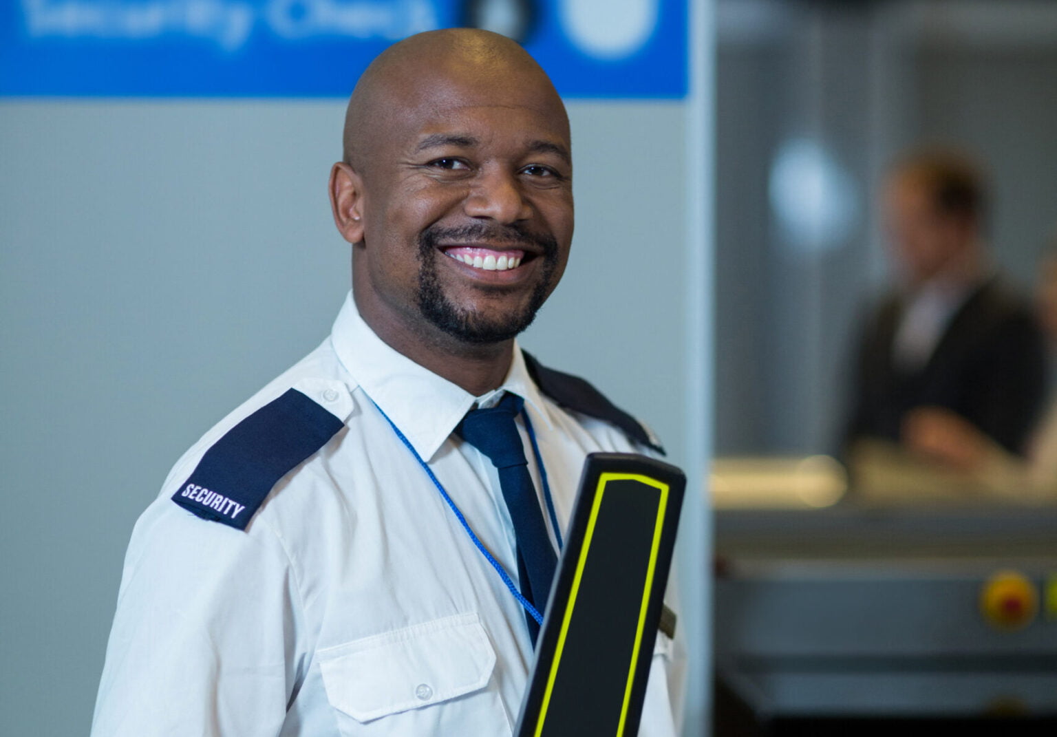 Portrait of smiling airport security officer holding metal detector in ...